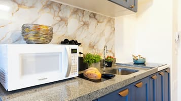 Uma cozinha com micro-ondas branco, bancada de granito, armários azuis, painel de mármore e pia.