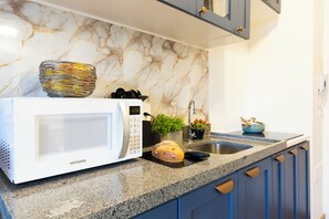 Uma cozinha com micro-ondas branco, bancada de granito, armários azuis, painel de mármore e pia.