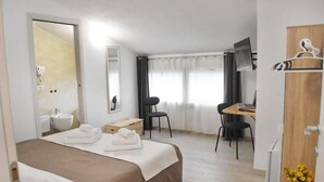 Quarto de hotel com cama, escrivaninha, cadeira, televisão e guarda-roupa.