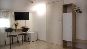 Um quarto pequeno com uma escrivaninha, duas cadeiras, uma televisão, um guarda-roupa e uma estante de madeira.