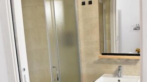 Casa de banho moderna com cabine de duche em vidro, lavatório branco e espelho em cima.