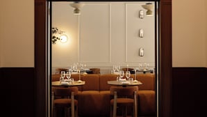 Entrada de um restaurante com uma placa que diz 'BISTRO DOONDER'. No interior, mesas montadas com copos e talheres, e um sofá é visível ao fundo.