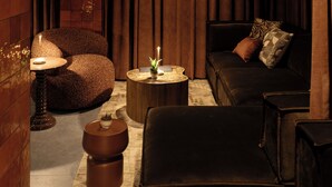 Um quarto com iluminação suave, um sofá, uma mesa de centro redonda e uma mesinha lateral com uma vela.