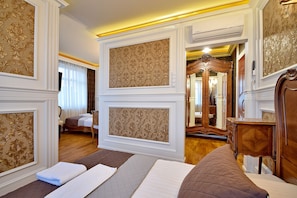 Quarto de hotel com uma cama grande, um espaço de estar com uma poltrona, uma penteadeira com espelho e um espelho grande no canto.