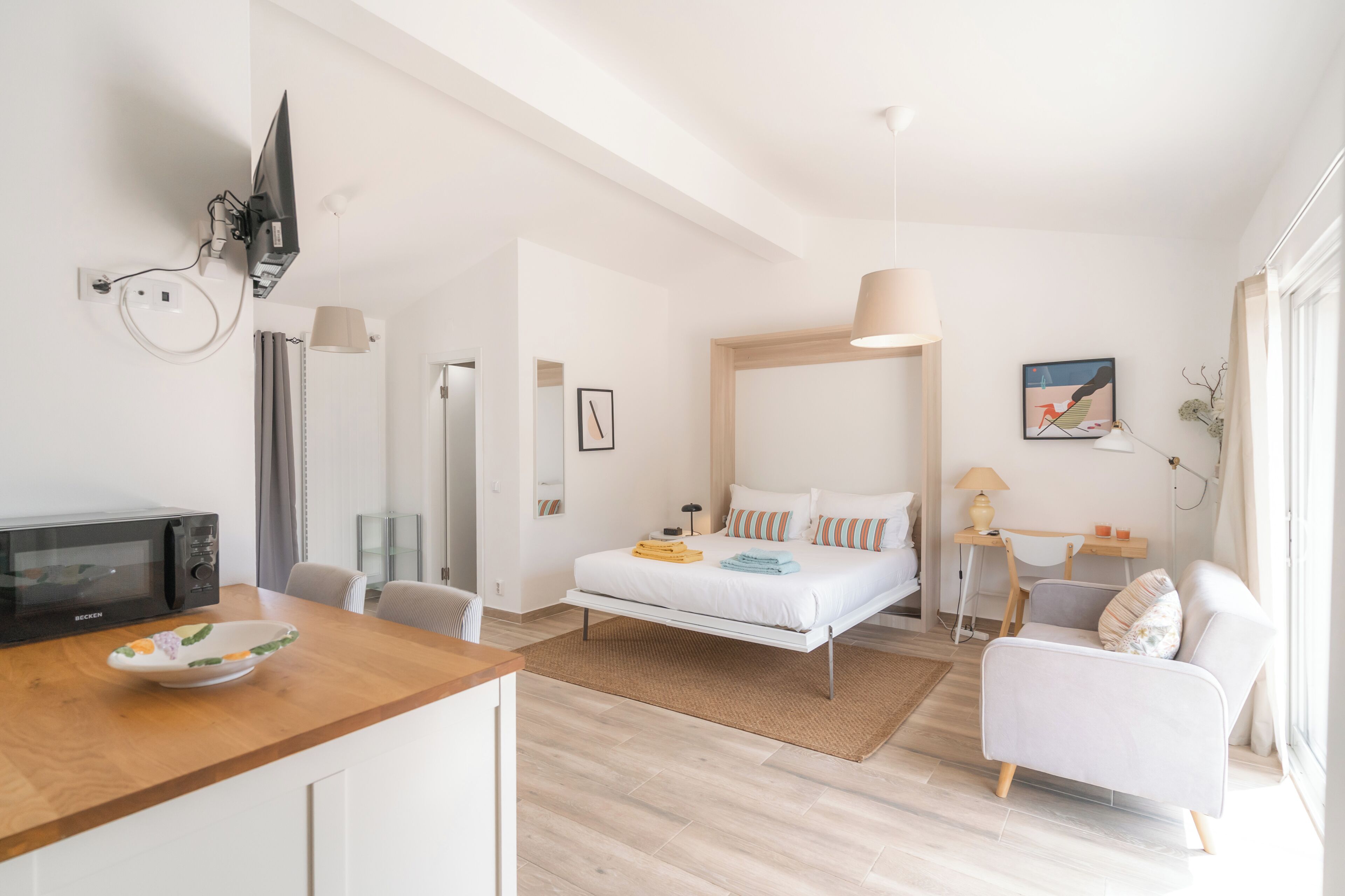 Quarto de hotel moderno com cama, escrivaninha, cadeira, micro-ondas, televisão e janela.
