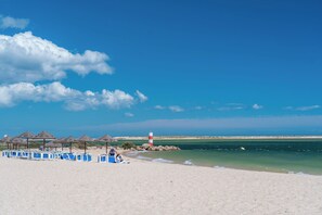 Uma praia com guarda-sóis, cadeiras de praia e um farol.