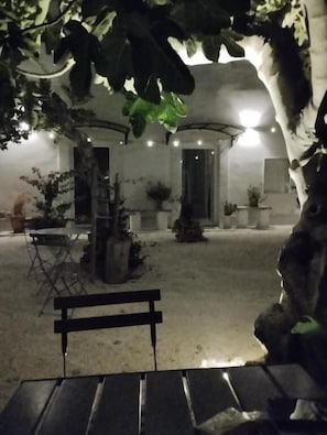 Área externa com banco, plantas em vasos e uma parede de pedra.