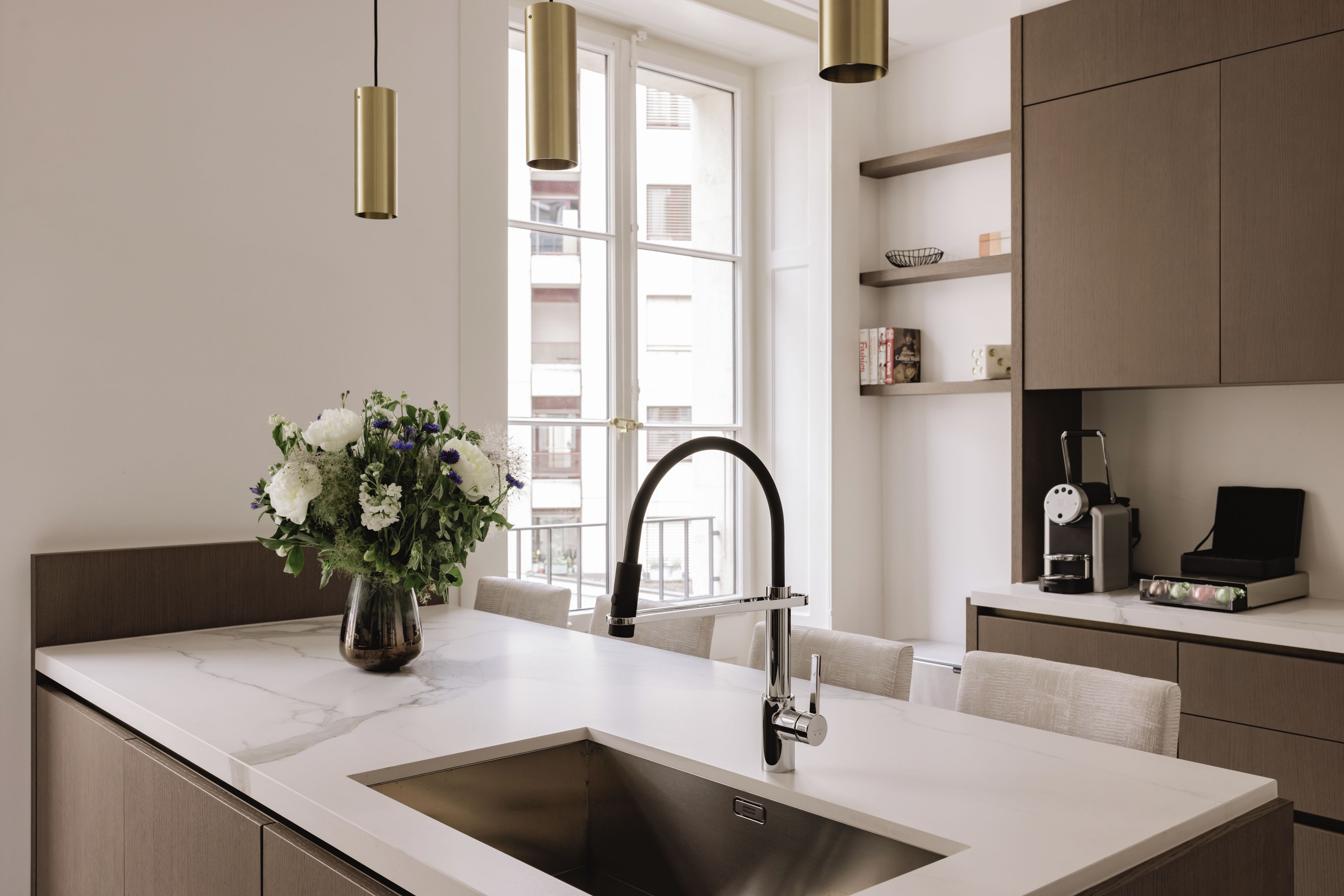 Cozinha moderna com ilha central, pia de aço inoxidável e iluminação pendente.