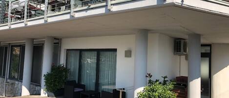 Um hotel com área externa coberta para acomodação, janelas amplas e vasos de plantas.