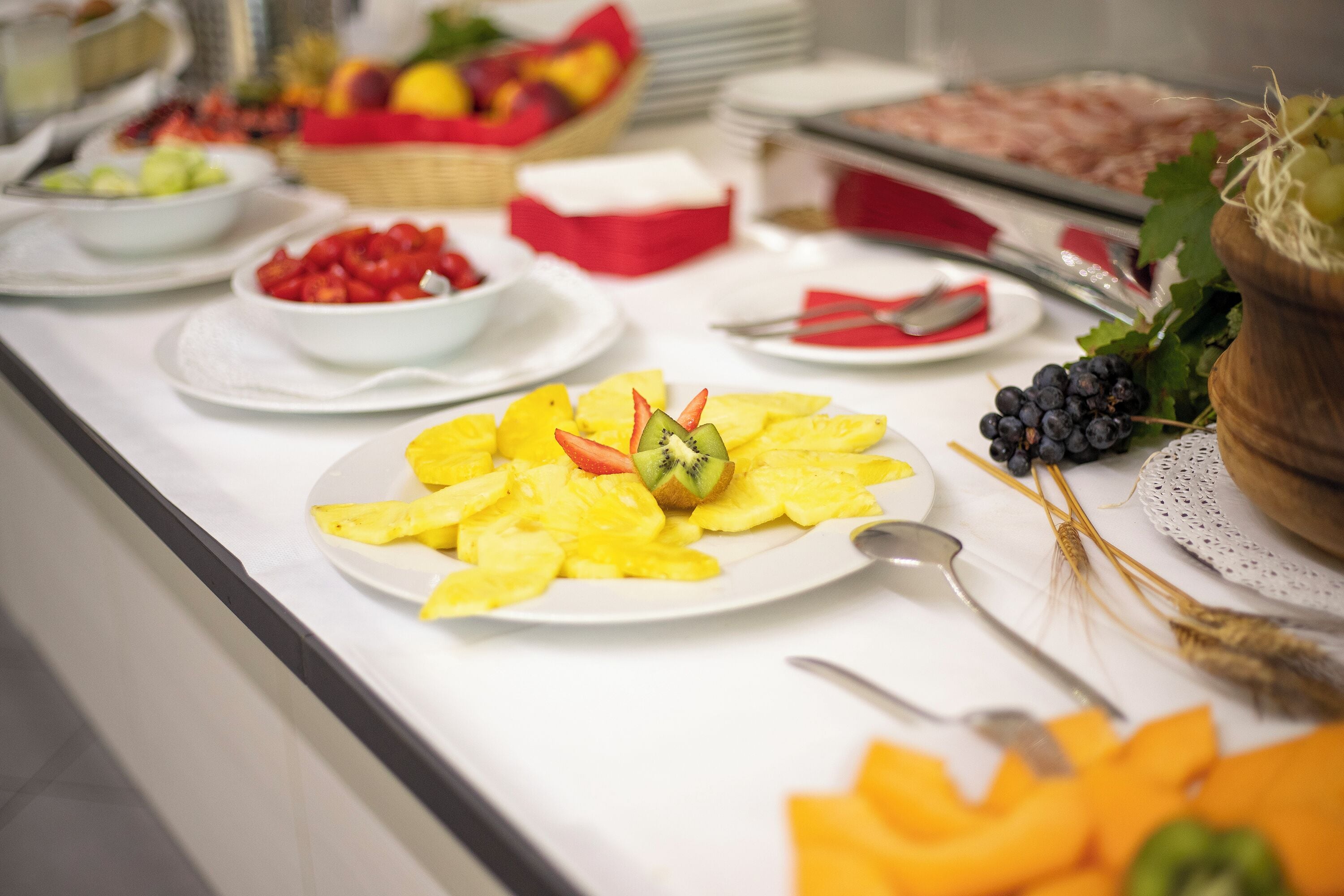 Uma mesa de buffet com diversas frutas e uma tigela de madeira com uvas.