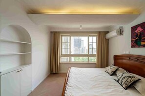 Quarto com cama, janela com cortinas, ar-condicionado fixado na parede e um quadro.