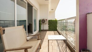 Uma varanda com um banco, uma mesa e vista para a cidade.