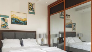 Quarto de hotel com uma cama grande, uma mesa de cabeceira, um espelho e obras de arte nas paredes.