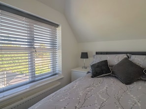 Quarto com cama, mesa de cabeceira, luminária e janela com persianas.