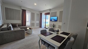 Uma sala de estar moderna com sofá, mesa de jantar com cadeiras, televisão na parede e varanda com vista.