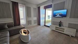Uma sala de estar com sofá, televisão, mesa de centro e uma porta de vidro deslizante para área externa.