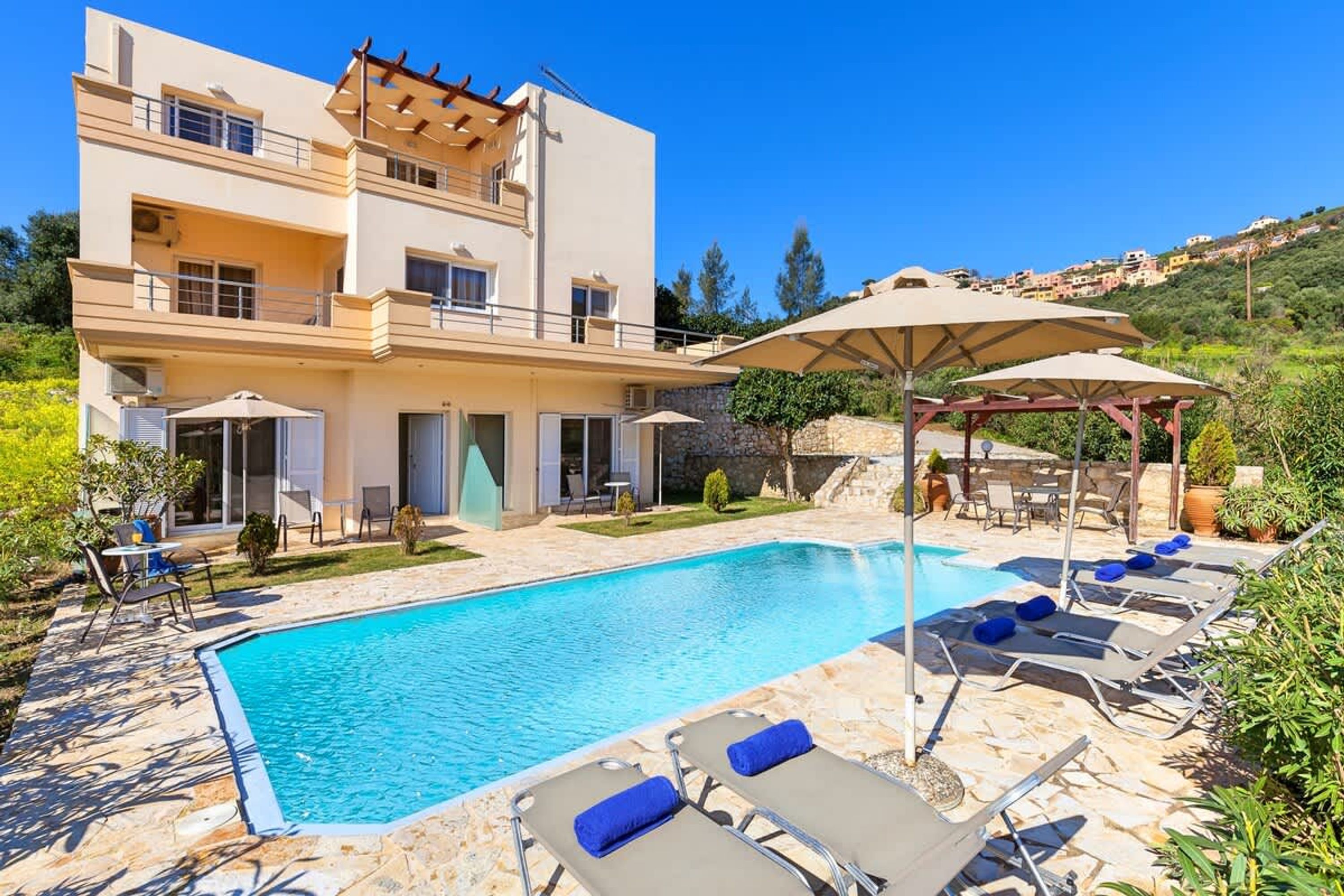 Um edifício moderno de dois andares com piscina, espreguiçadeiras e área de estar ao ar livre.