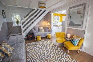 Um espaço de estar compacto com sofá, poltronas, um tapete estampado, escada e área de cozinha.