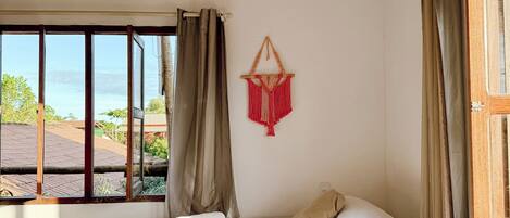 Quarto com cama, janela e decoração de macramé pendurada na parede.