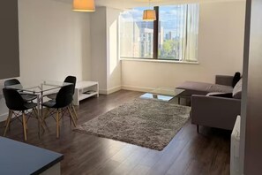 Uma sala de estar moderna com uma mesa de vidro para refeições, duas cadeiras, um sofá, uma mesa de centro e uma janela grande com vista para a cidade.