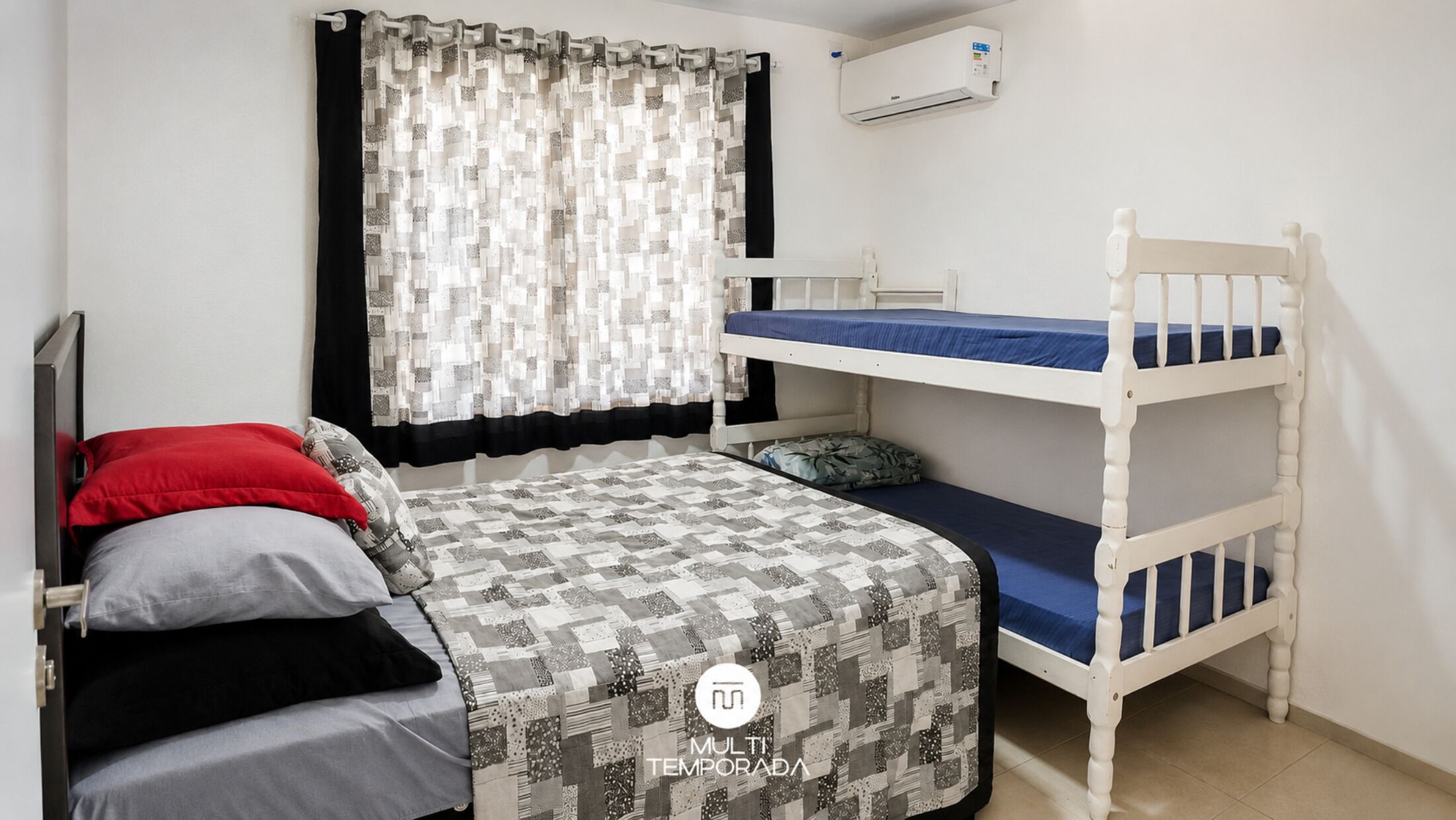 Quarto com beliche, cama de solteiro e janela com cortinas estampadas.