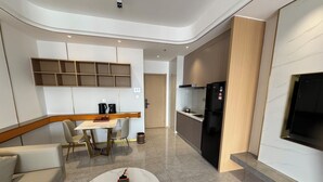Uma sala de estar moderna com sofá, mesa de centro, TV e área de cozinha com geladeira e armários.
