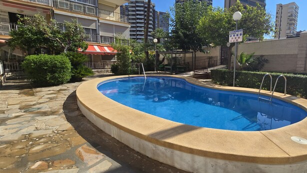 Piscina com borda de pedra, rodeada por vegetação e edifícios.