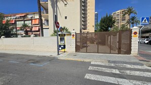 Vista da rua mostrando uma faixa de pedestres, placa de proibido estacionar, um caixa eletrônico e entrada gradeada para um edifício.
