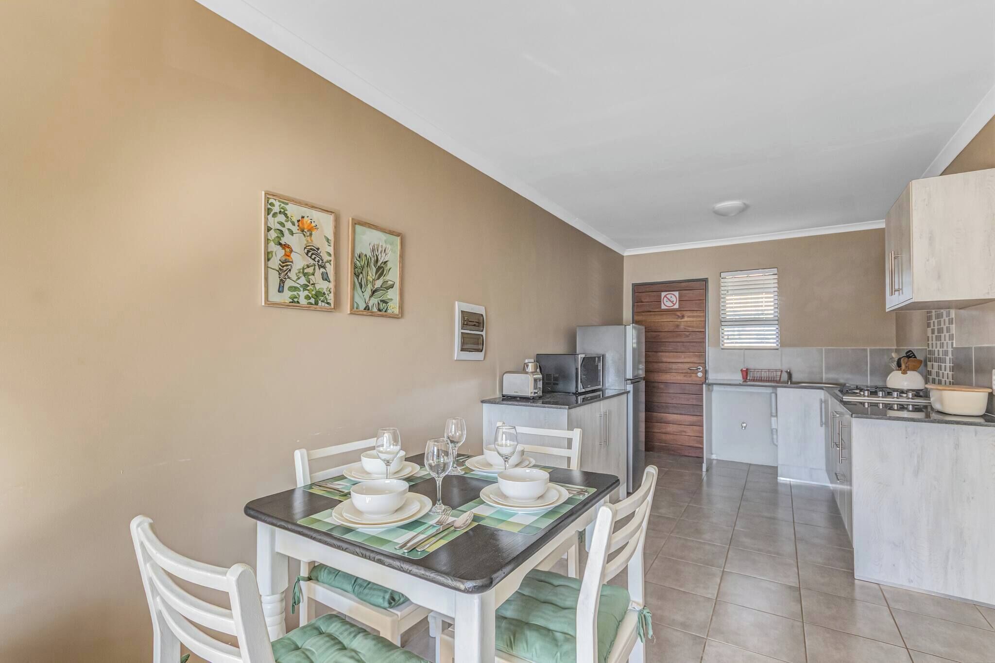 Uma sala de jantar com mesa posta para quatro pessoas, uma cozinha com eletrodomésticos modernos e uma porta com placa de 'Proibido Entrar'.