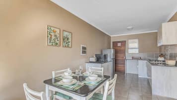 Uma sala de jantar com mesa posta para quatro pessoas, uma cozinha com eletrodomésticos modernos e uma porta com placa de 'Proibido Entrar'.