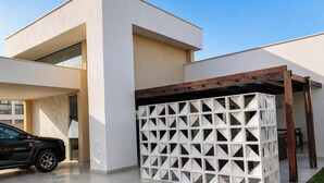 Um edifício moderno com garagem, um carro estacionado em frente e uma estrutura de treliça branca.