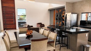 Cozinha moderna com ilha central, área de refeições com cadeiras e lixeira à vista.