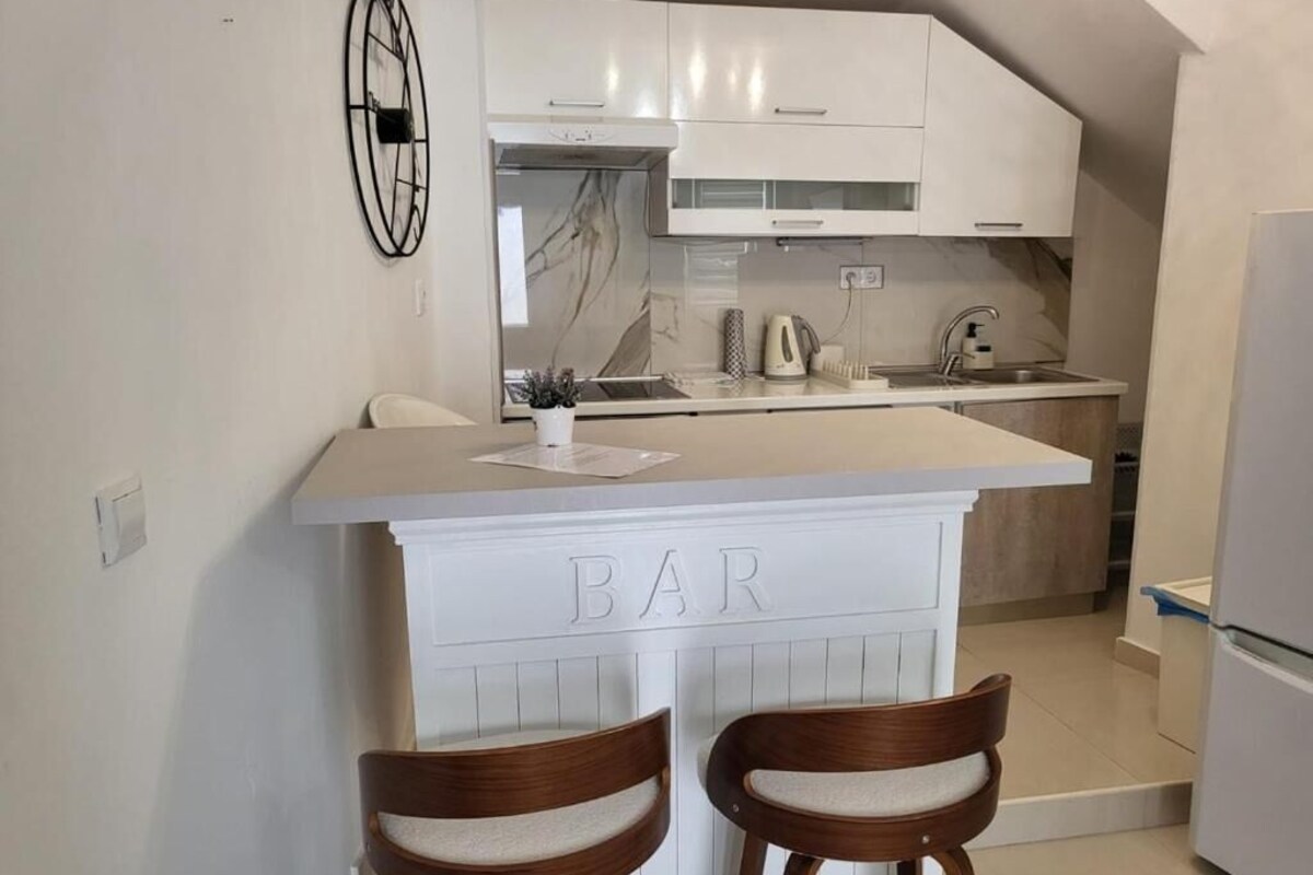 Cozinha com área de bar, armários brancos e dois banquetas de madeira.