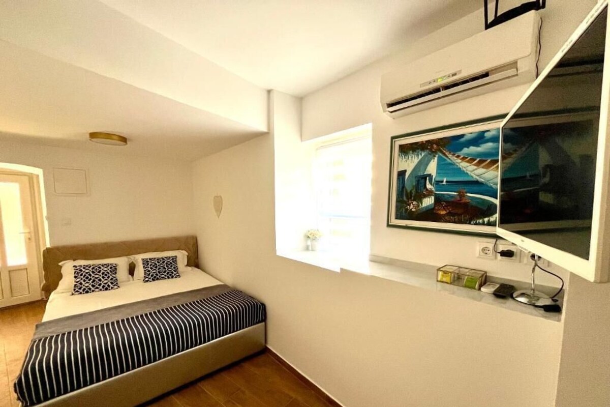 Um quarto com uma cama, uma janela, um ar condicionado e um quadro na parede.
