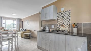 Uma cozinha moderna com armários cinza, painel de azulejos e um espaço de refeições com sofá e mesa.