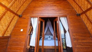 Quarto de madeira com uma cama, janela com cortinas e vista para o exterior.