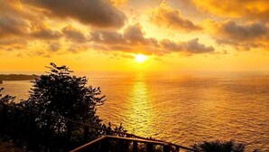 Um pôr do sol sobre a água, com um corrimão em primeiro plano.