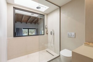 Uma casa de banho moderna com um claraboia, cabine de duche em vidro, sanita e lavatório embutido.