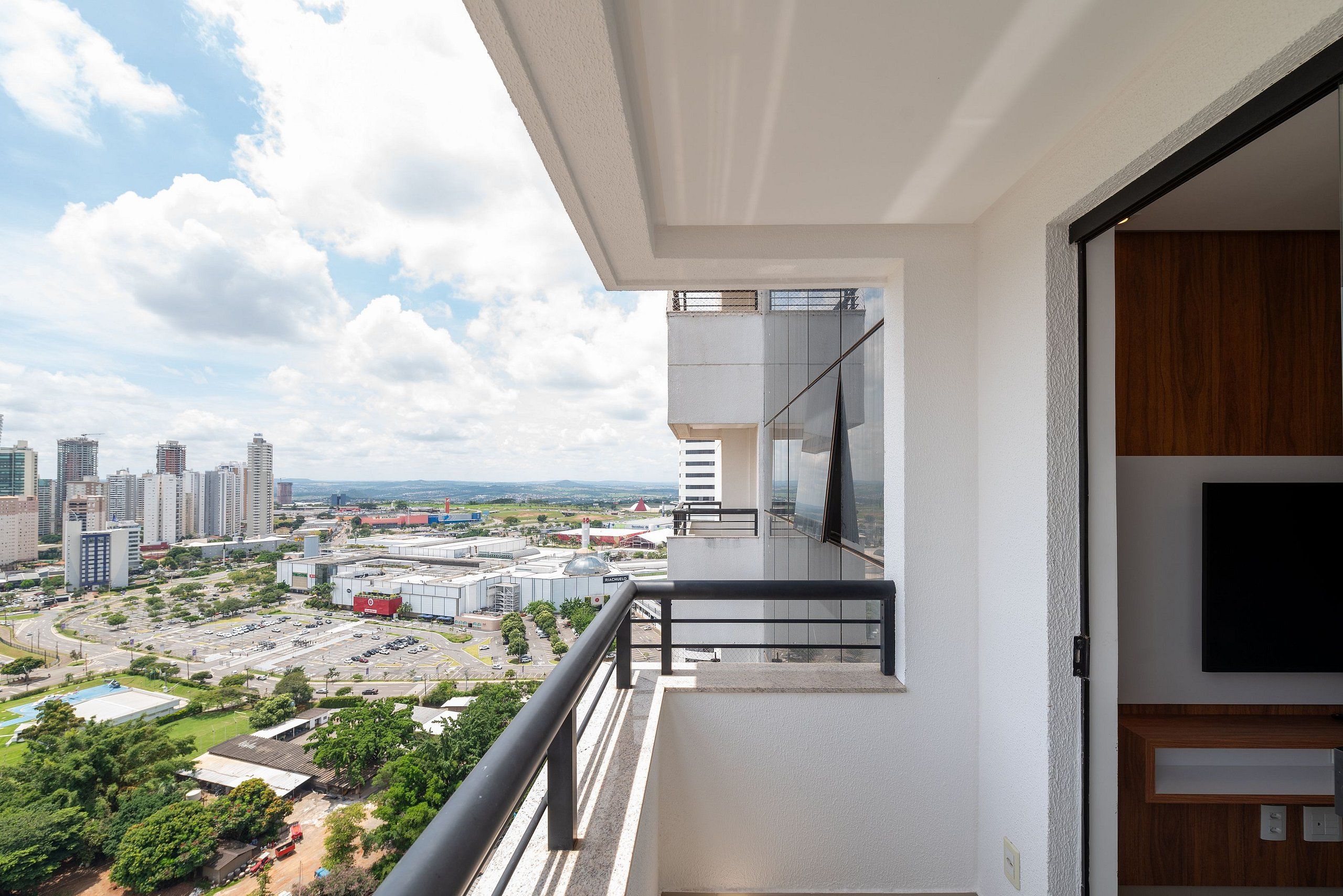 Uma varanda com vista para a cidade, uma televisão na parede e uma porta que dá para o interior.