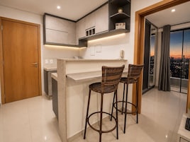 Uma cozinha moderna com área de bar, dois banquetes de vime, prateleira embutida e vista para a cidade através de uma grande janela.