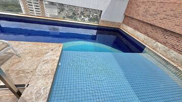 Piscina com bordas azulejadas, uma cadeira de metal e uma parede de tijolos.