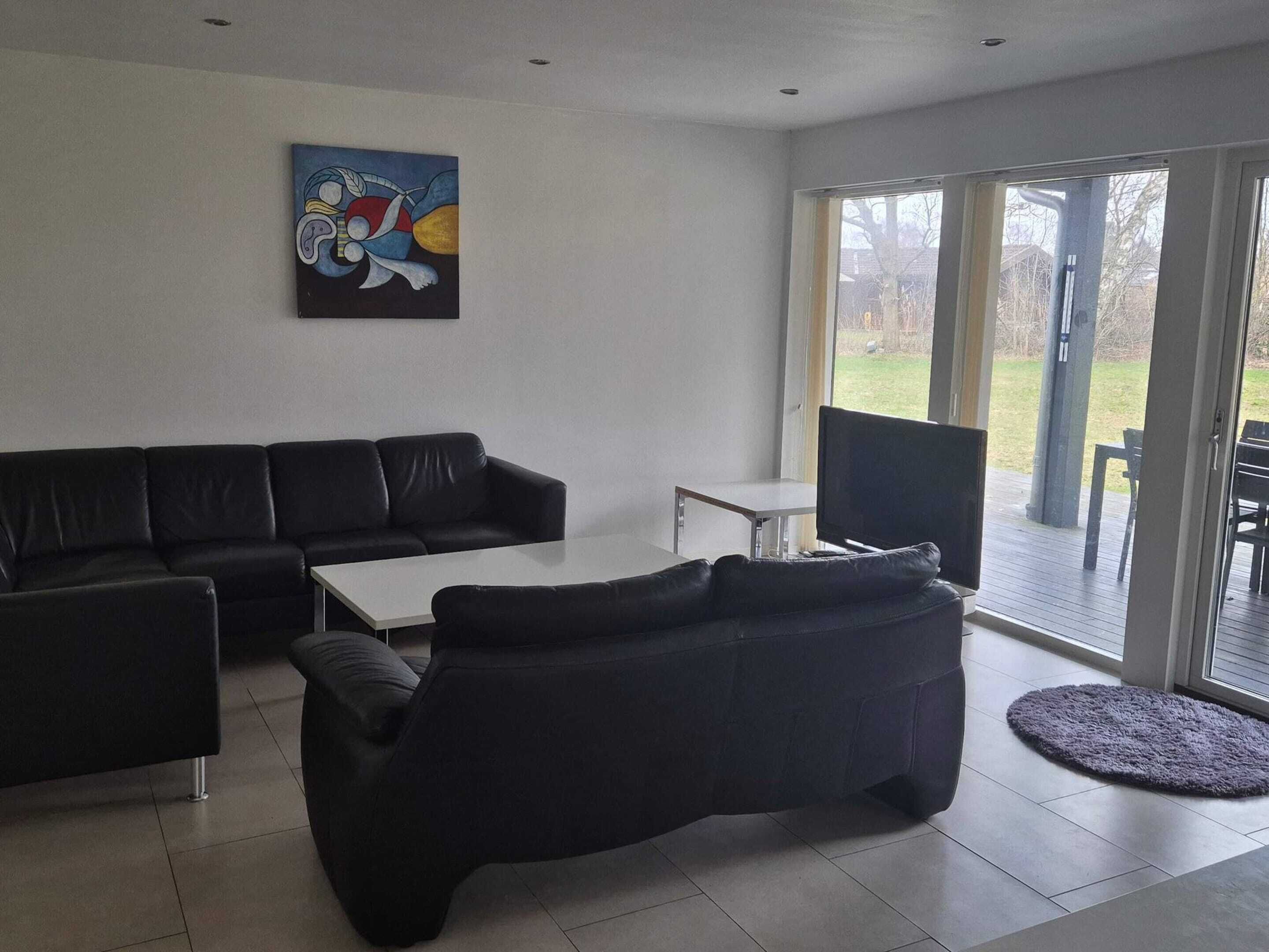Uma sala de estar moderna com um sofá de couro preto, uma mesa de centro branca e uma pintura na parede.