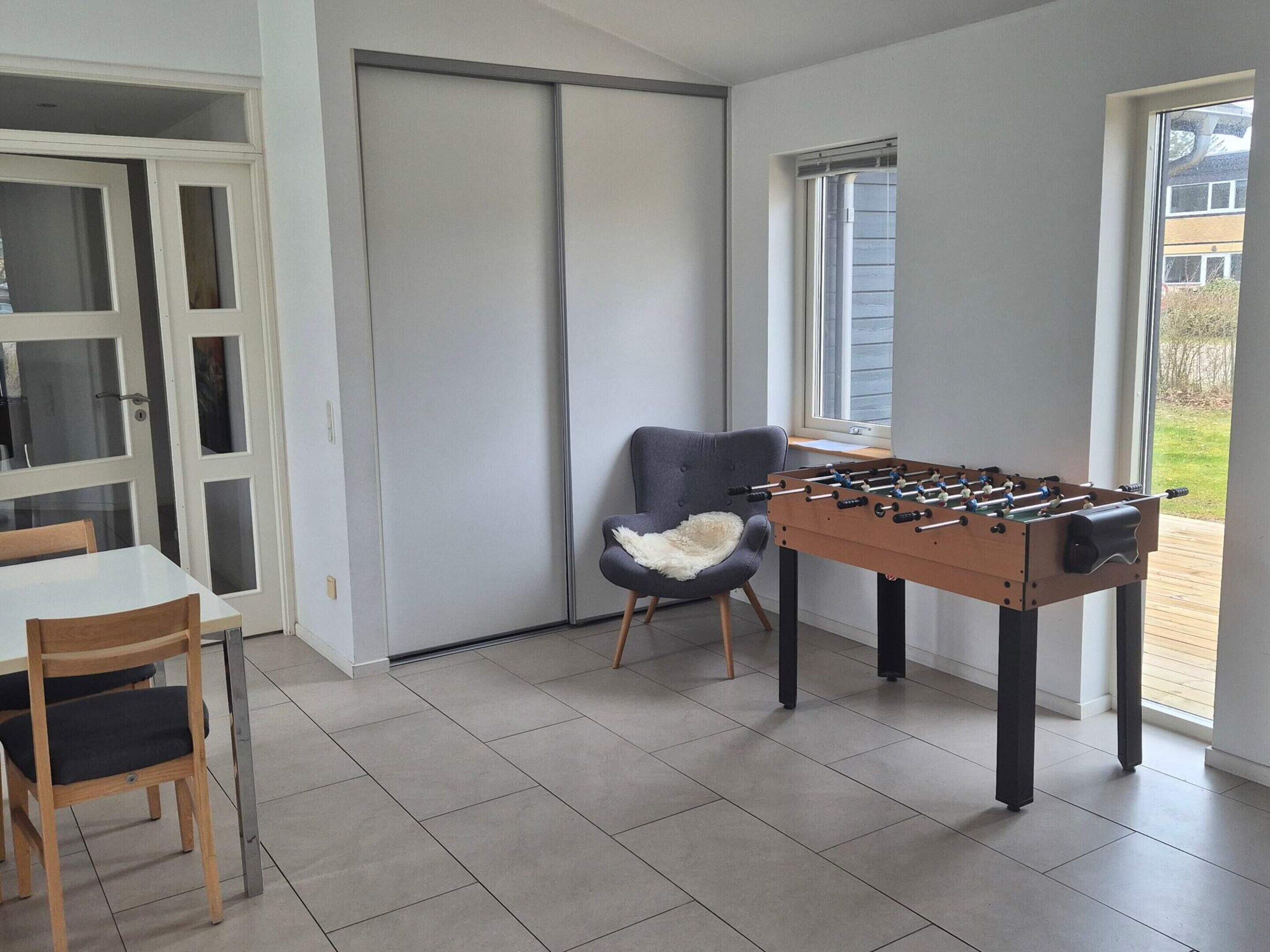 Quarto com mesa de futebol, uma cadeira, uma mesa e uma porta deslizante.