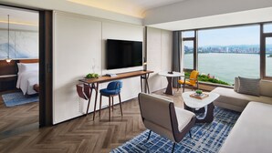 Quarto de hotel moderno com uma grande janela, televisão de tela plana, sofá, mesa de jantar e uma pequena cozinha.
