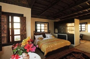 Quarto com cama, mesa de cabeceira, vaso com flores e janela.
