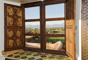 Um quarto com chão xadrez, uma janela grande com vista para uma paisagem e um armário de madeira com detalhes elaborados.
