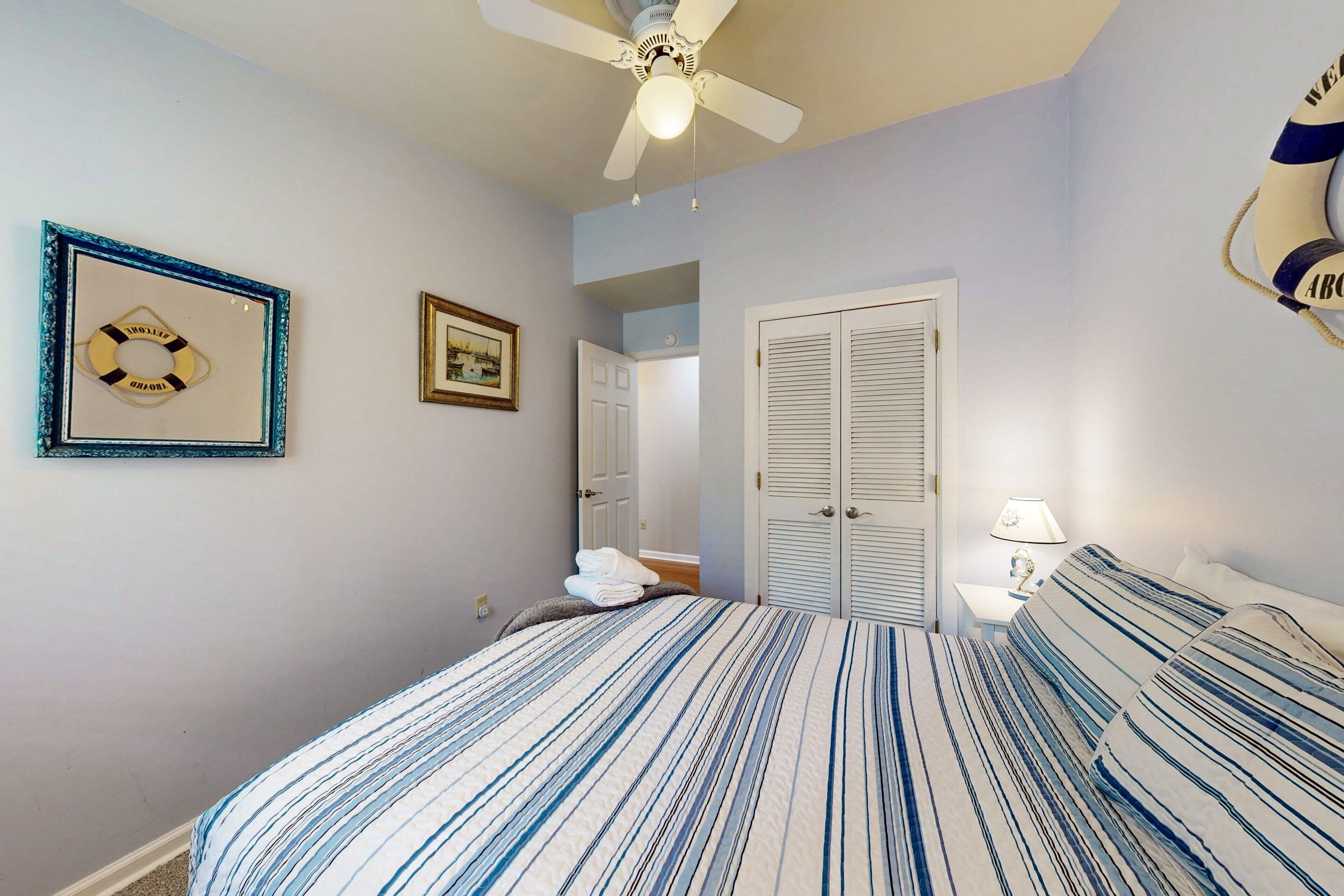 Quarto com cama, ventoinha no teto, decoração com boia salva-vidas e uma porta.