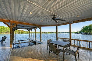 Um deck coberto com mesa e cadeiras, uma piscina e vista para a água.