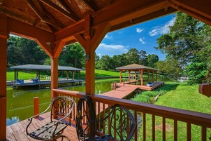 Um deck de madeira com cadeiras e um banco, com vista para um lago com barcos, cercado por vegetação exuberante.