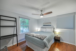 Quarto com cama, ventilador de teto, janela, mesa de cabeceira e prateleira.